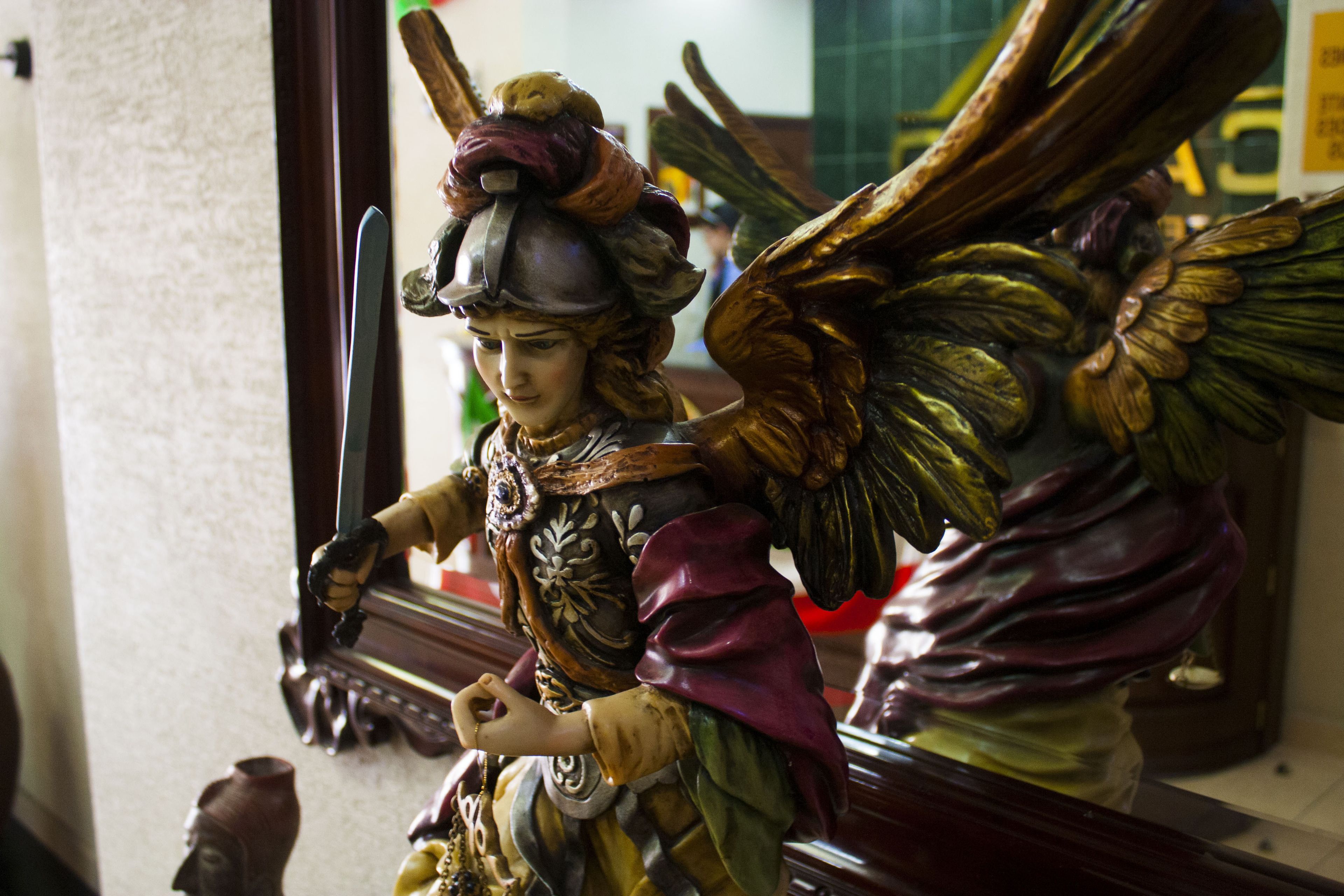 Estátua de um anjo com espada, colocada em frente a um espelho.