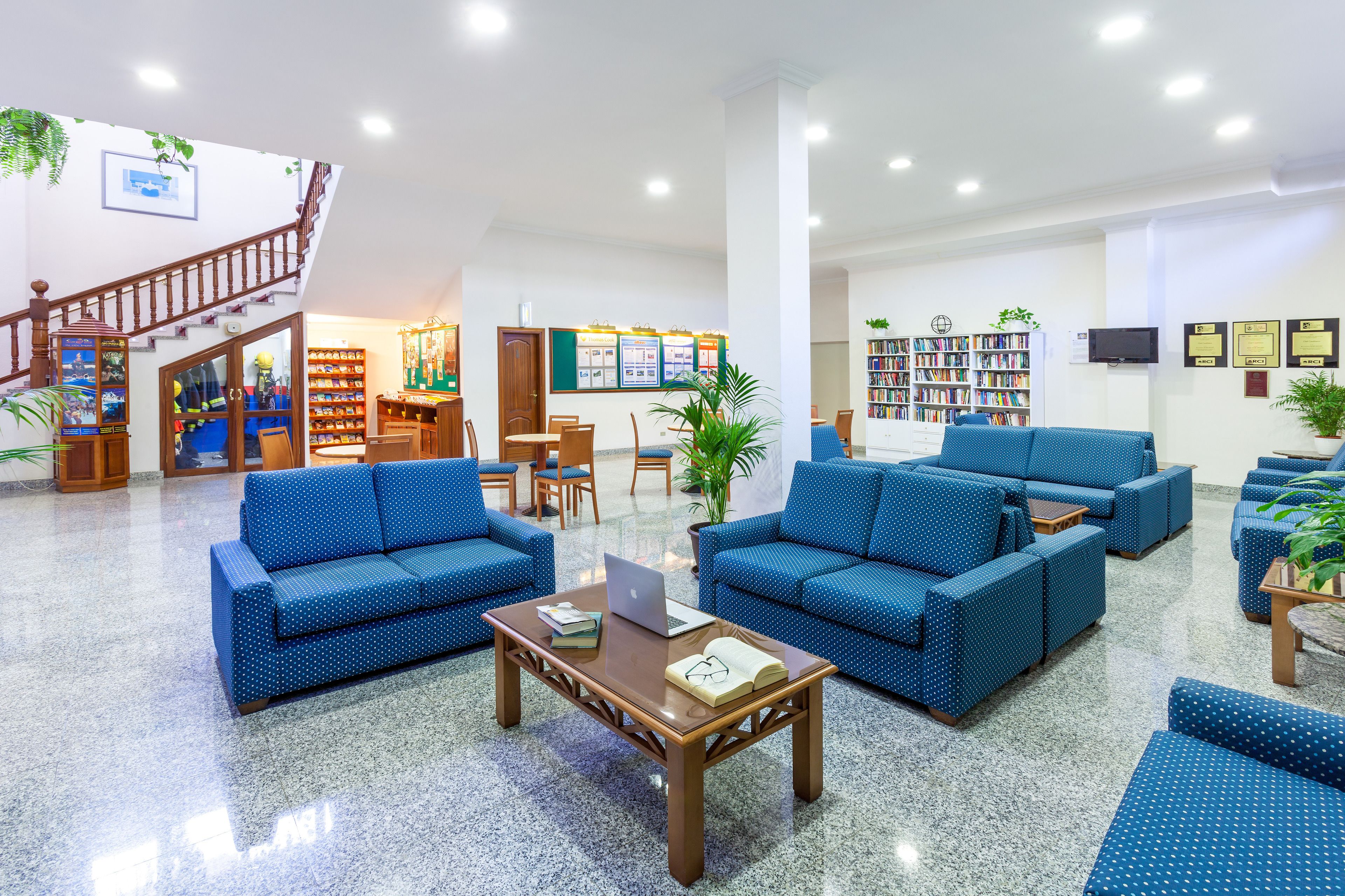 Um hall amplo com sofás estampados em azul, uma mesa de centro de madeira e uma escada que leva a um andar superior.