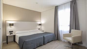 Quarto de hotel com cama, mesas de cabeceira, uma cadeira e janela com cortinas.