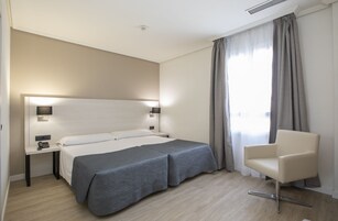 Quarto de hotel com cama, mesas de cabeceira, uma cadeira e janela com cortinas.