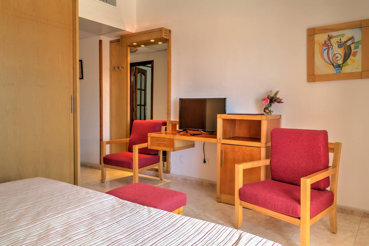 Quarto com cama, escrivaninha com cadeira, televisão e um quadro na parede.
