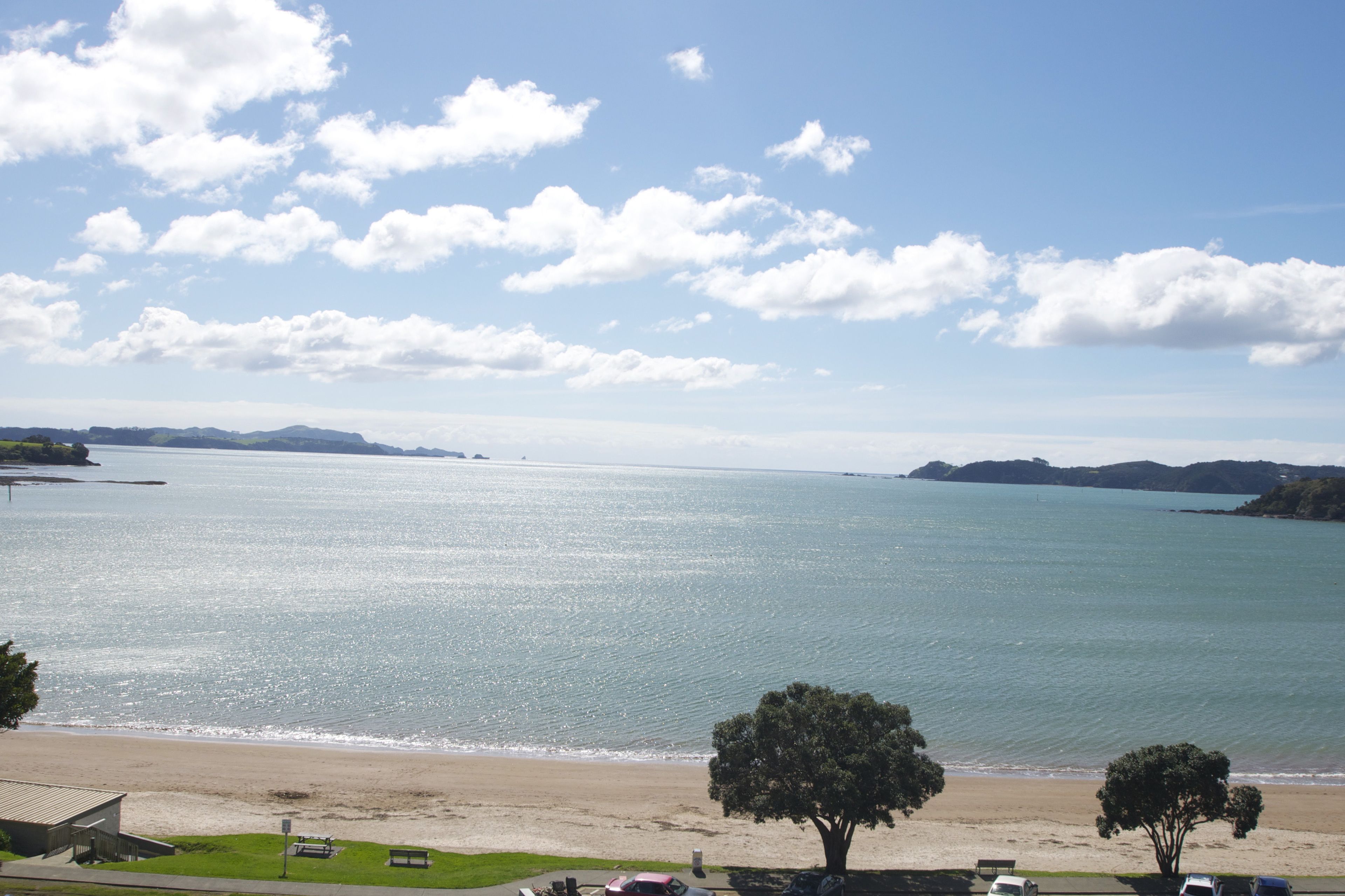 Vista costeira com praia, árvores e céu claro.