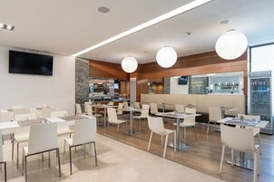 Um restaurante moderno com várias mesas e cadeiras, espaço de bar e uma tela grande na parede.