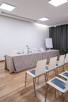 Sala de conferência com uma mesa comprida, cadeiras, quadro branco e tela de projeção.