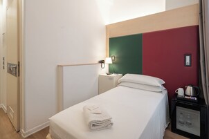 Quarto de hotel com uma cama, mesa de cabeceira com abajur, telefone e pequeno armário.