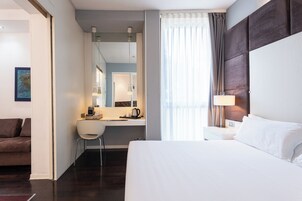 Quarto de hotel com cama, escrivaninha, cadeira, máquina de café e luminária.