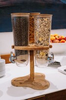 Um distribuidor de alimentos com três compartimentos contendo diferentes tipos de grãos e sementes.
