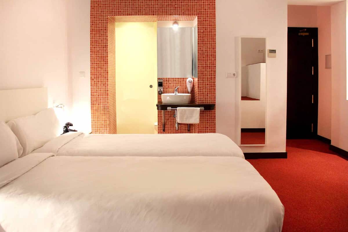 Quarto de hotel com uma cama grande, banheiro com pia e espelho, e um tapete vermelho.