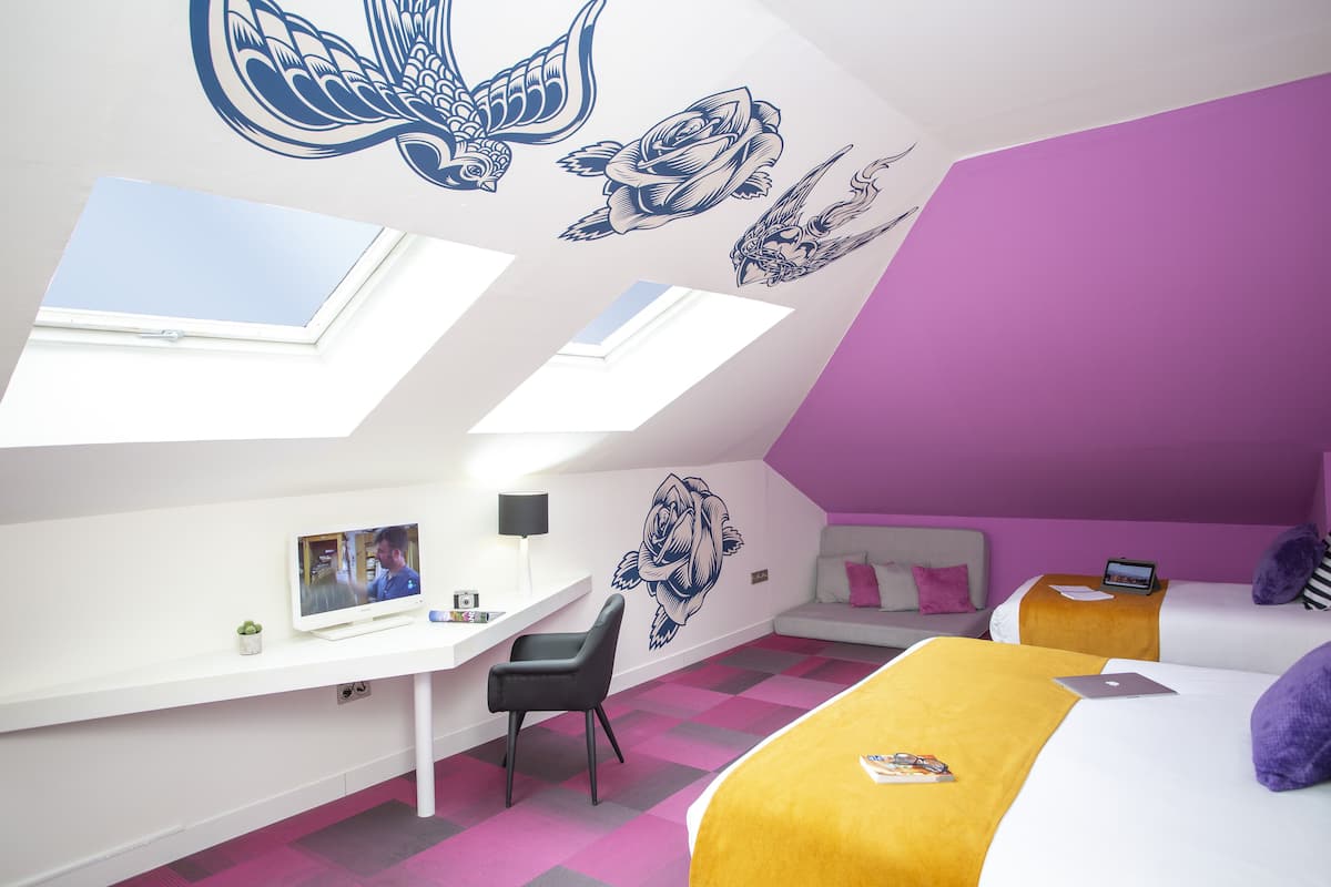 Quarto moderno com claraboias, uma escrivaninha, uma cadeira, duas camas e um grande mural na parede.