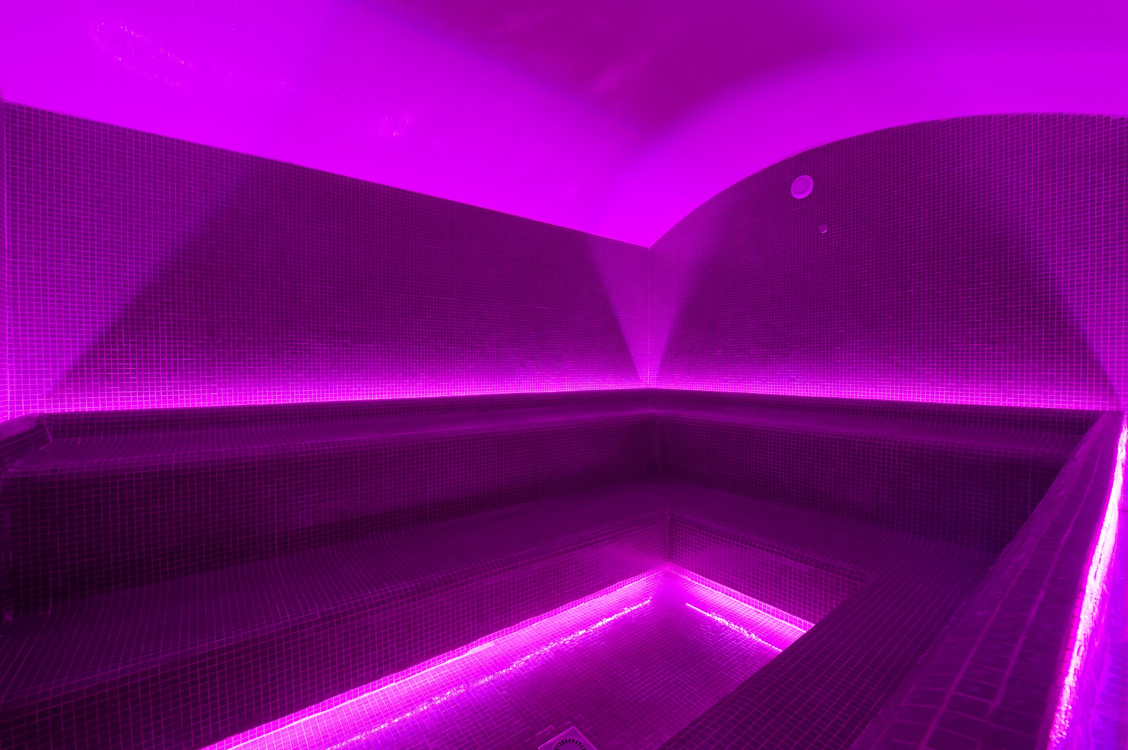 Um spa moderno com design geométrico em azulejos e iluminação roxa.