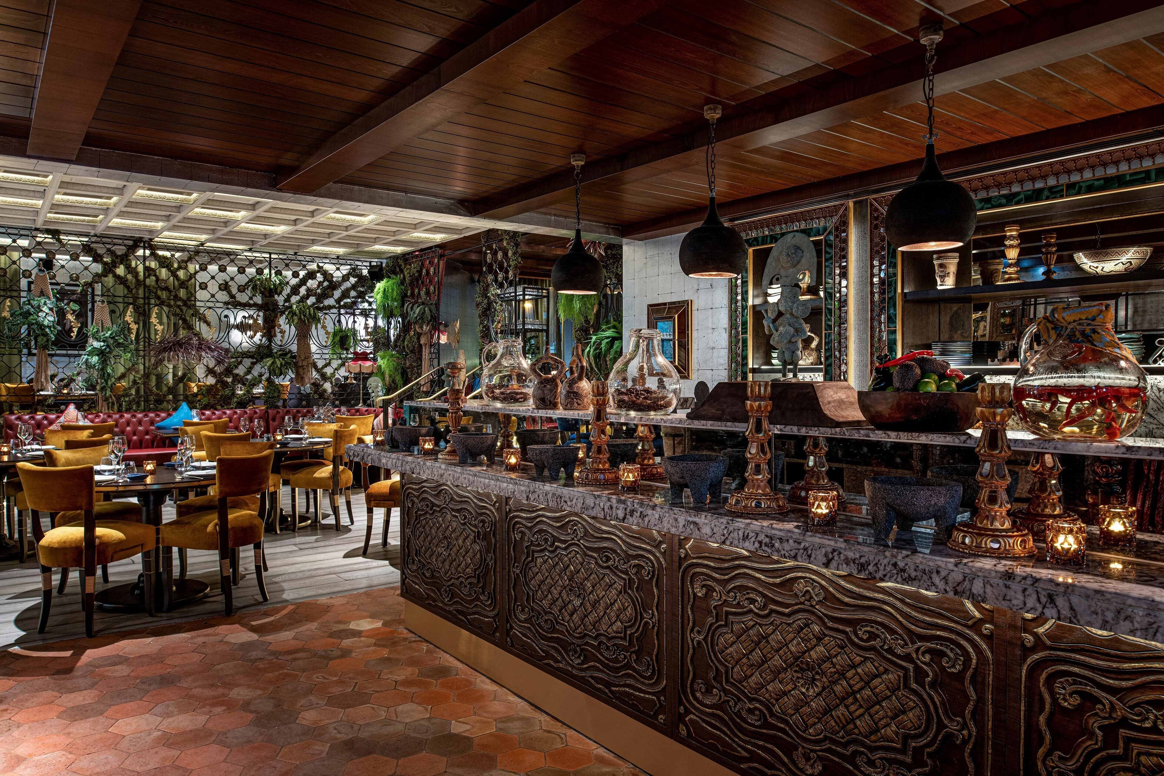 Restaurante com teto de madeira, chão de terracota e área de bar com decorações e iluminação detalhadas.