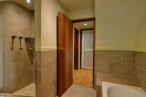 Casa de banho com chuveiro, banheira e porta de madeira que dá para outro quarto.