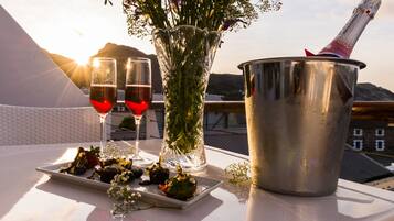 Uma mesa com uma garrafa de champanhe, duas taças de vinho tinto, um vaso de flores e um prato de comida.