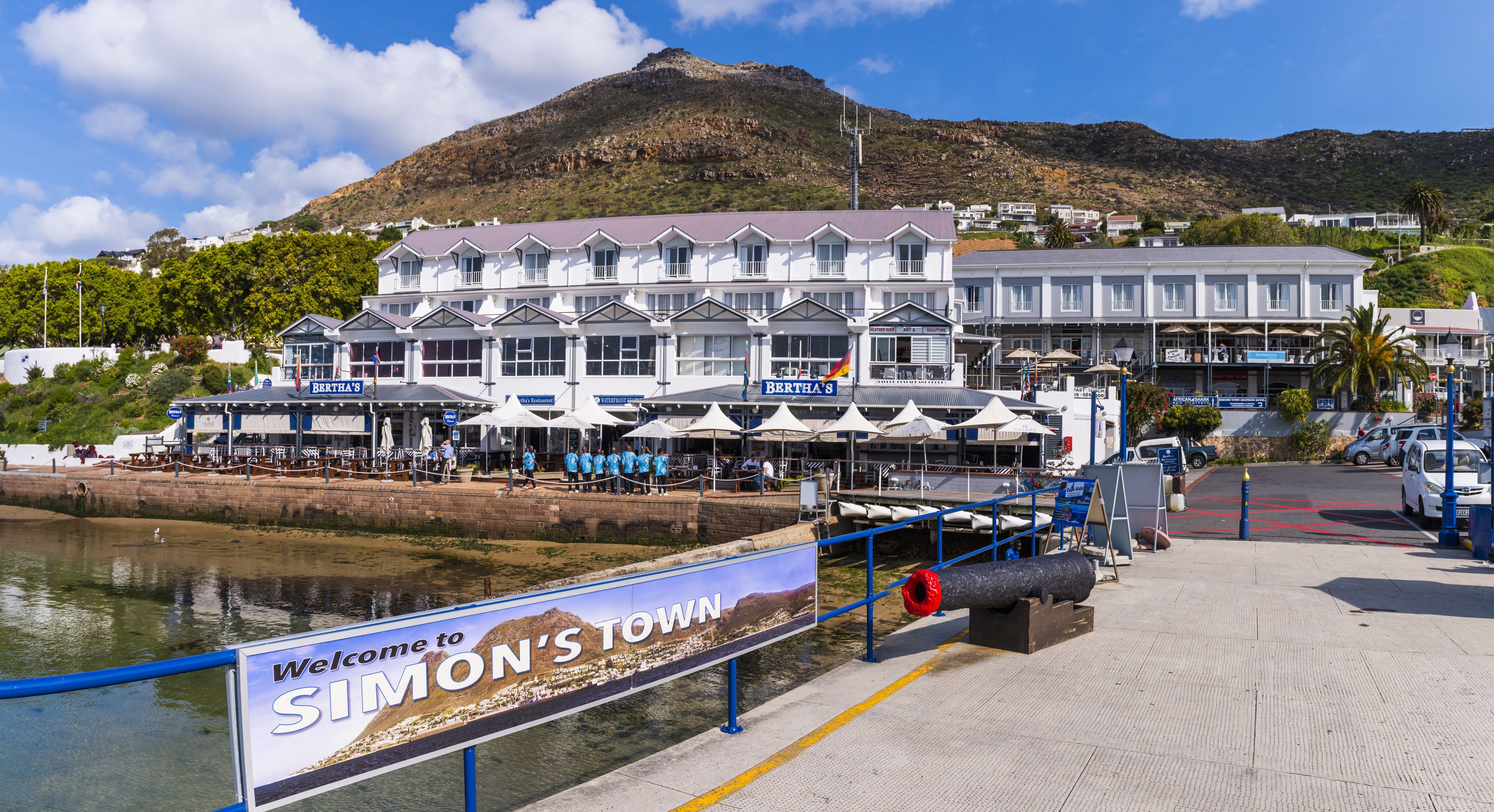 Um hotel à beira-mar com várias varandas, área de estar ao ar livre e uma placa de boas-vindas a Simon's Town.