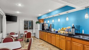 Cozinha moderna com armários de madeira, bancada preta e parede azul decorativa. Há várias luminárias pendentes, uma geladeira e uma pia.