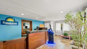Uma área de recepção com parede azul, balcão de recepção, balcão, púlpito iluminado em azul, um banco de madeira, um sofá e uma planta em vaso.