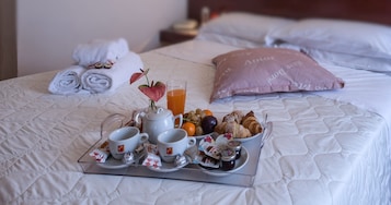 Cama bem arrumada com bandeja de itens de café da manhã, incluindo croissants, frutas e um copo de suco de laranja.