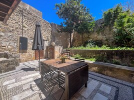 Um pátio de paredes de pedra com uma mesa e cadeiras de madeira, um vaso de planta e um banco de pedra.