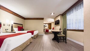 Quarto de hotel com duas camas, uma mesa de jantar, televisão e janela com cortinas.