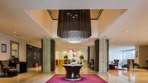 Um hall espaçoso com um lustre central, um balcão de recepção e uma área de estar com cadeiras.
