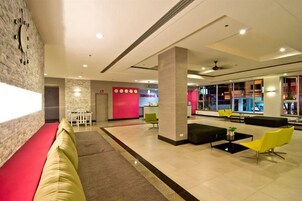 Um lobby moderno com uma parede vermelha, área de estar com cadeiras amarelas e um pilar grande.