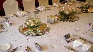 Mesa de jantar formal posta com toalha branca, talheres dourados e taças.