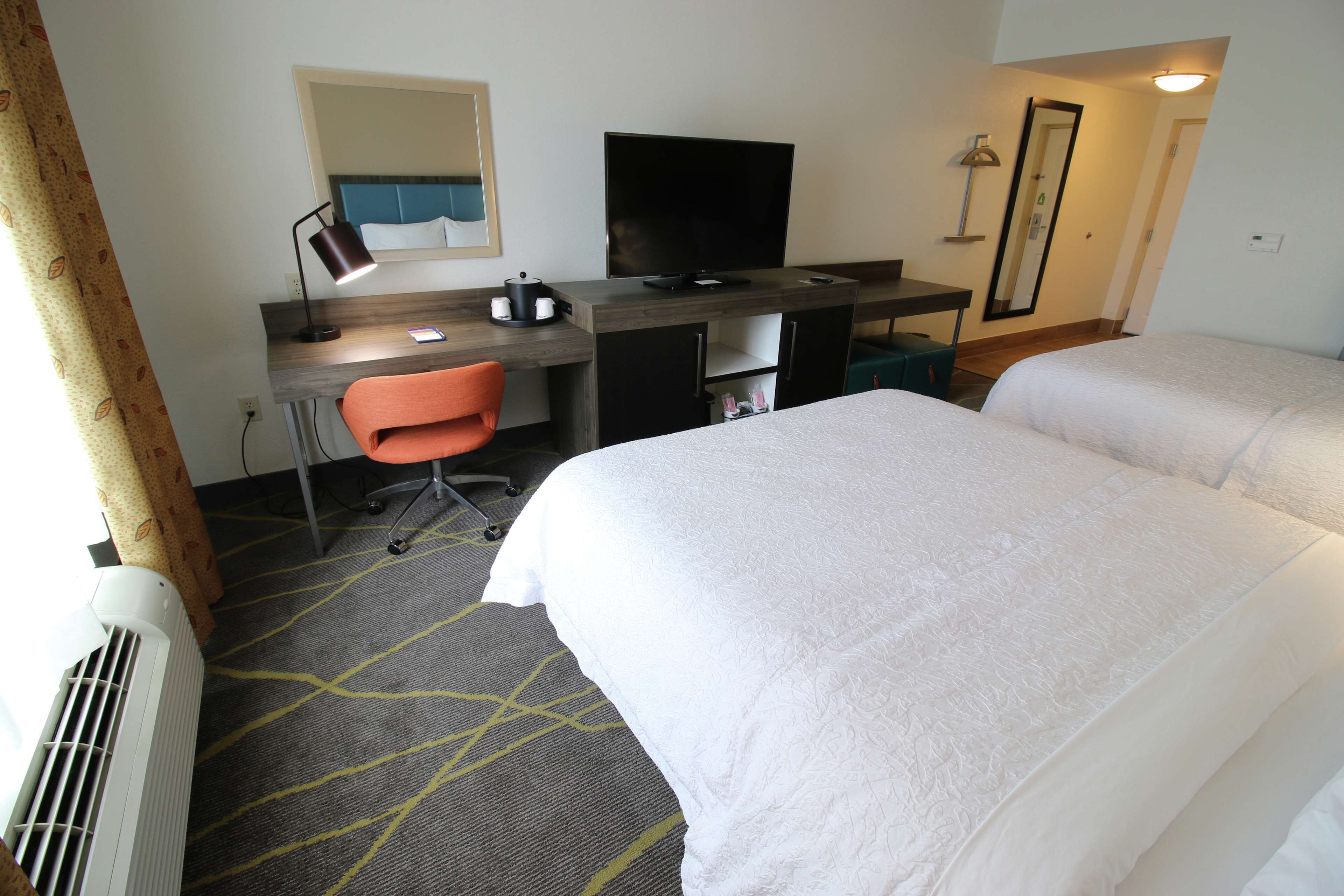 Quarto de hotel com duas camas, uma escrivaninha com computador, uma cadeira, televisão e espelho.