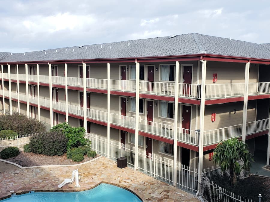 Um hotel com vários andares, varandas, piscina e um jardim ajardinado.