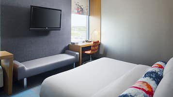 Quarto de hotel moderno com cama, escrivaninha, cadeira, televisão e janela com vista.