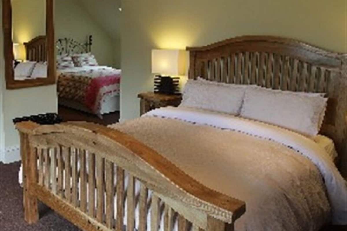 Uma cama de madeira com cabeceira, mesa de cabeceira e espelho na parede.
