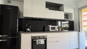 Uma cozinha moderna com geladeira preta, armários brancos, forno embutido e micro-ondas.