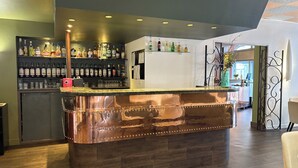 Uma área de bar com balcão de cobre, prateleiras cheias de garrafas de bebidas e piso de madeira.