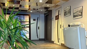 Um saguão de hotel com uma escada que dá acesso ao WC, uma receção e uma grande planta em vaso.