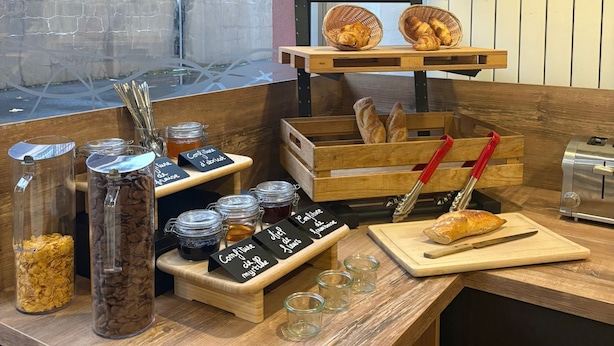 Um balcão de café com diversos produtos de pastelaria, potes de condimentos e uma planta pendente.