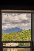 Vista através de uma janela de uma paisagem montanhosa, com um edifício ao primeiro plano.