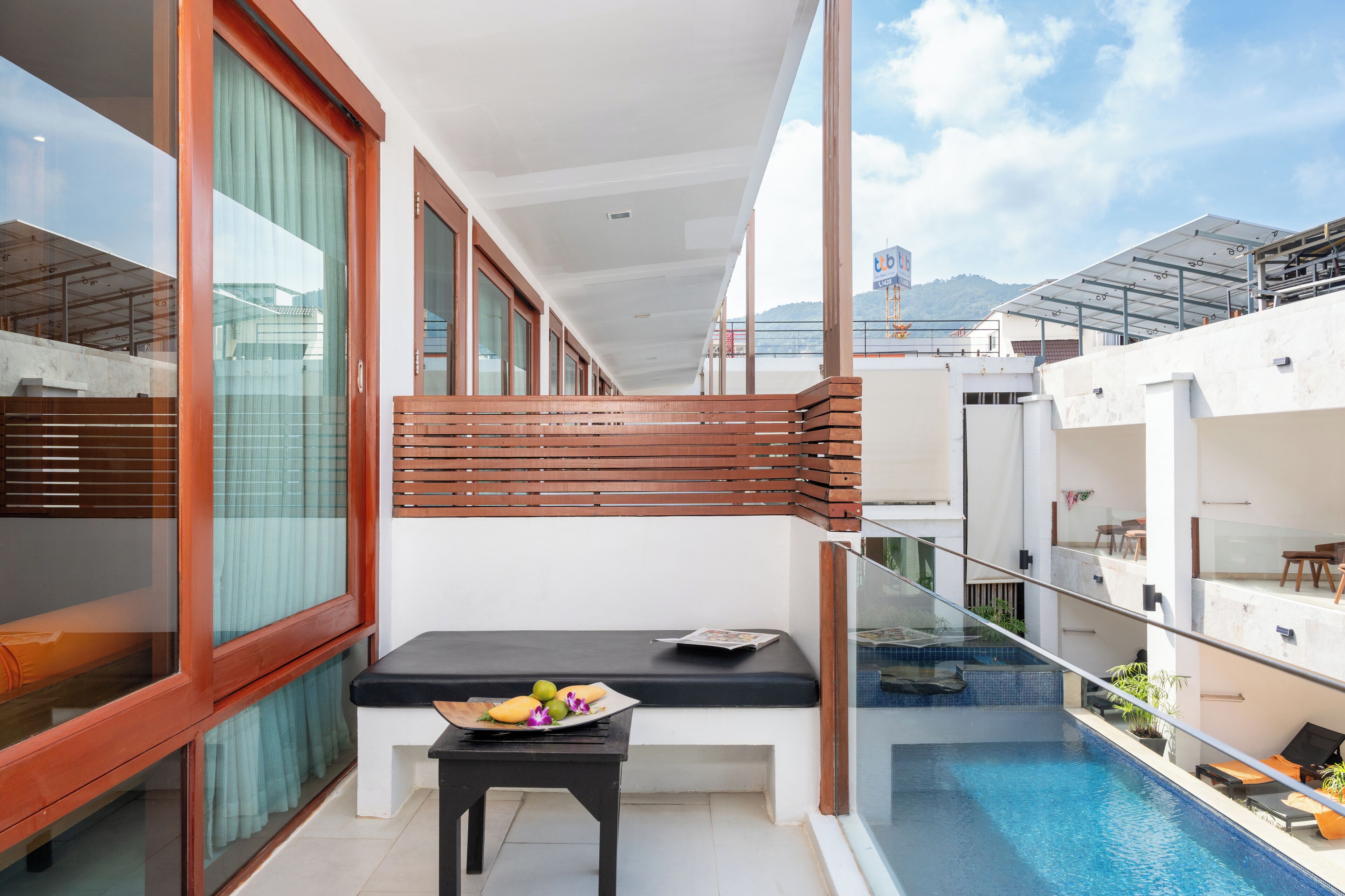 Uma varanda com piscina, divisória de madeira, um banco e uma mesa com uma travessa de fruta.