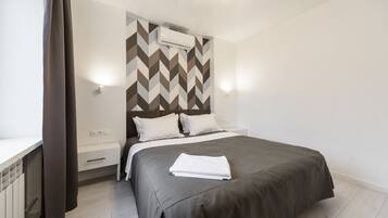 Quarto moderno com cama grande, cabeceira com padrão geométrico, mesa de cabeceira e ar condicionado fixado na parede.
