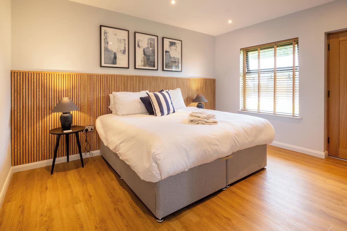 Quarto moderno com cama grande, cabeceira de madeira e janela com persianas.