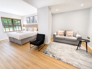Quarto moderno com cama, poltrona, sofá e mesa pequena.