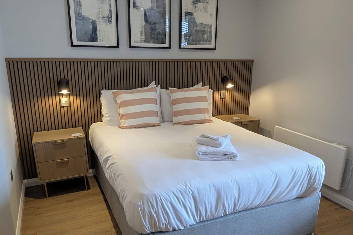 Quarto moderno com cama grande, cabeceira de madeira, mesas de cabeceira e luminárias fixadas na parede.