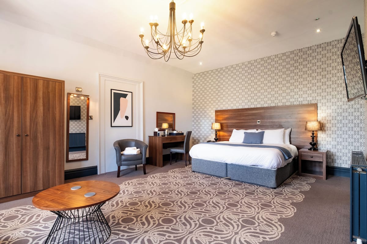 Quarto de hotel com uma cama grande, uma escrivaninha, uma cadeira, uma mesa de centro redonda e um guarda-roupa.