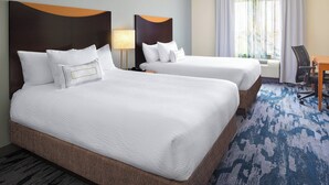 Quarto de hotel com duas camas, uma escrivaninha e uma cadeira.