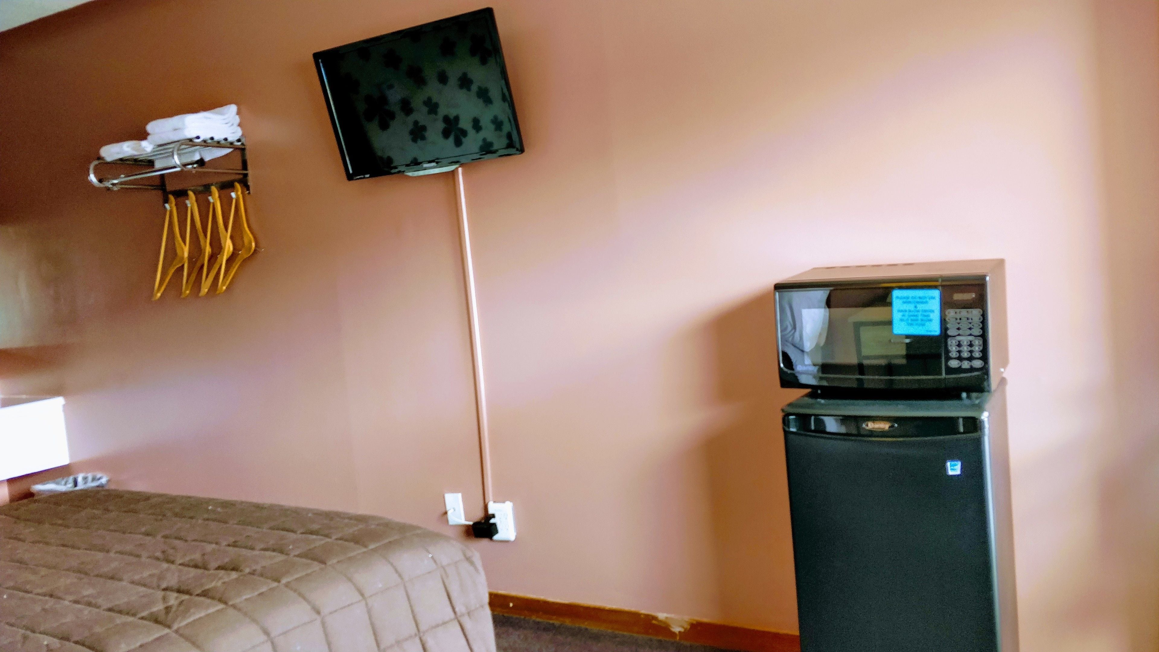 Quarto de hotel com cama, televisão fixada na parede e micro-ondas sobre um suporte.