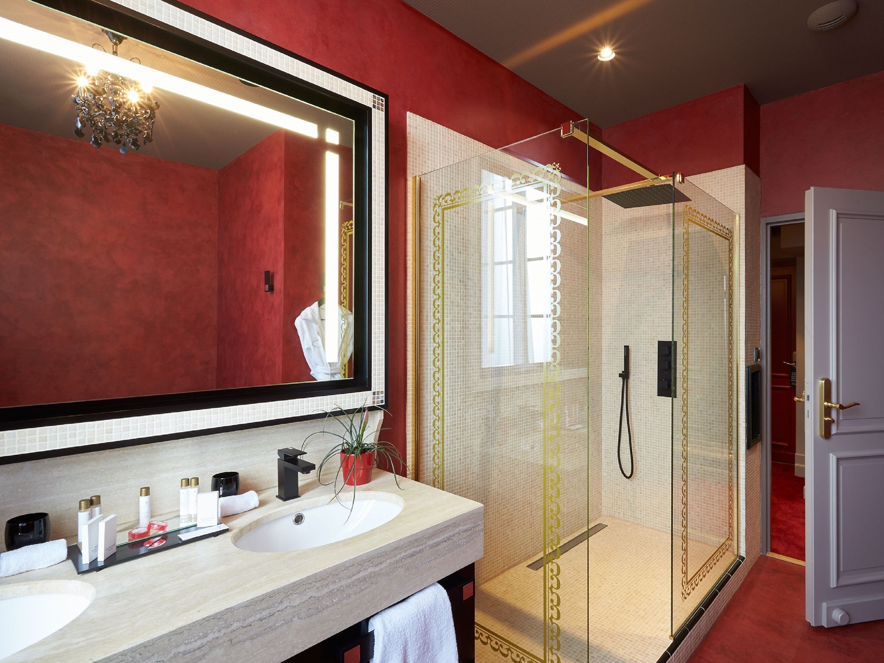 Casa de banho com um espelho grande, duas pias, chuveiro com portas de vidro e uma parede com detalhes em vermelho.