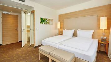 Quarto de hotel com duas camas, um banco, uma mesinha de cabeceira com telefone e uma luminária na parede.