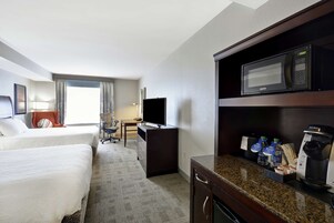 Quarto de hotel com duas camas, uma escrivaninha, televisão, micro-ondas, cafeteira e minibar.