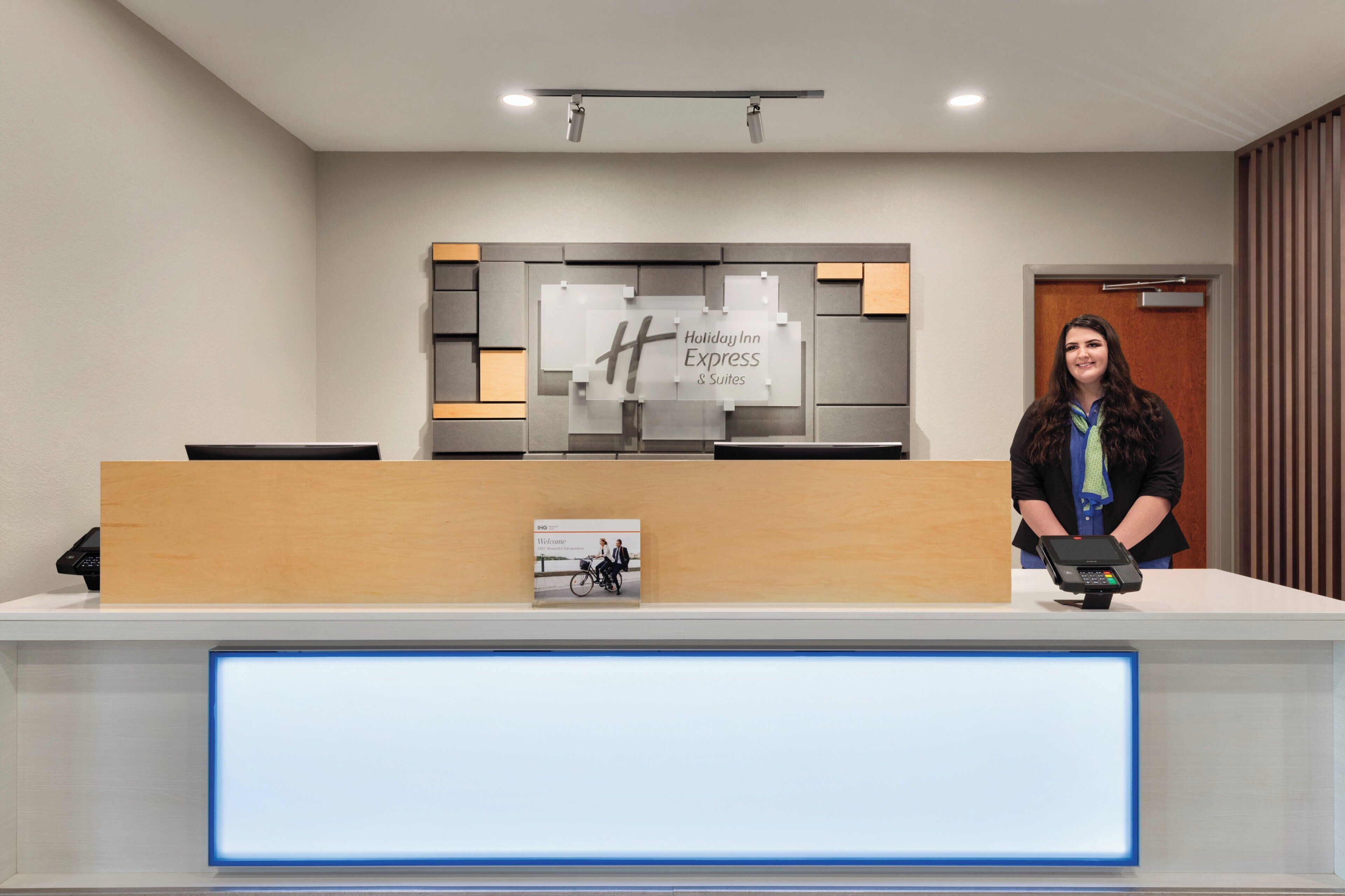 Balcão de recepção com placa da Holiday Inn Express & Suites, uma câmera de segurança instalada e um display digital.