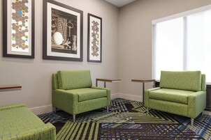 Quarto com duas poltronas verdes, um tapete estampado e três obras de arte emolduradas na parede.
