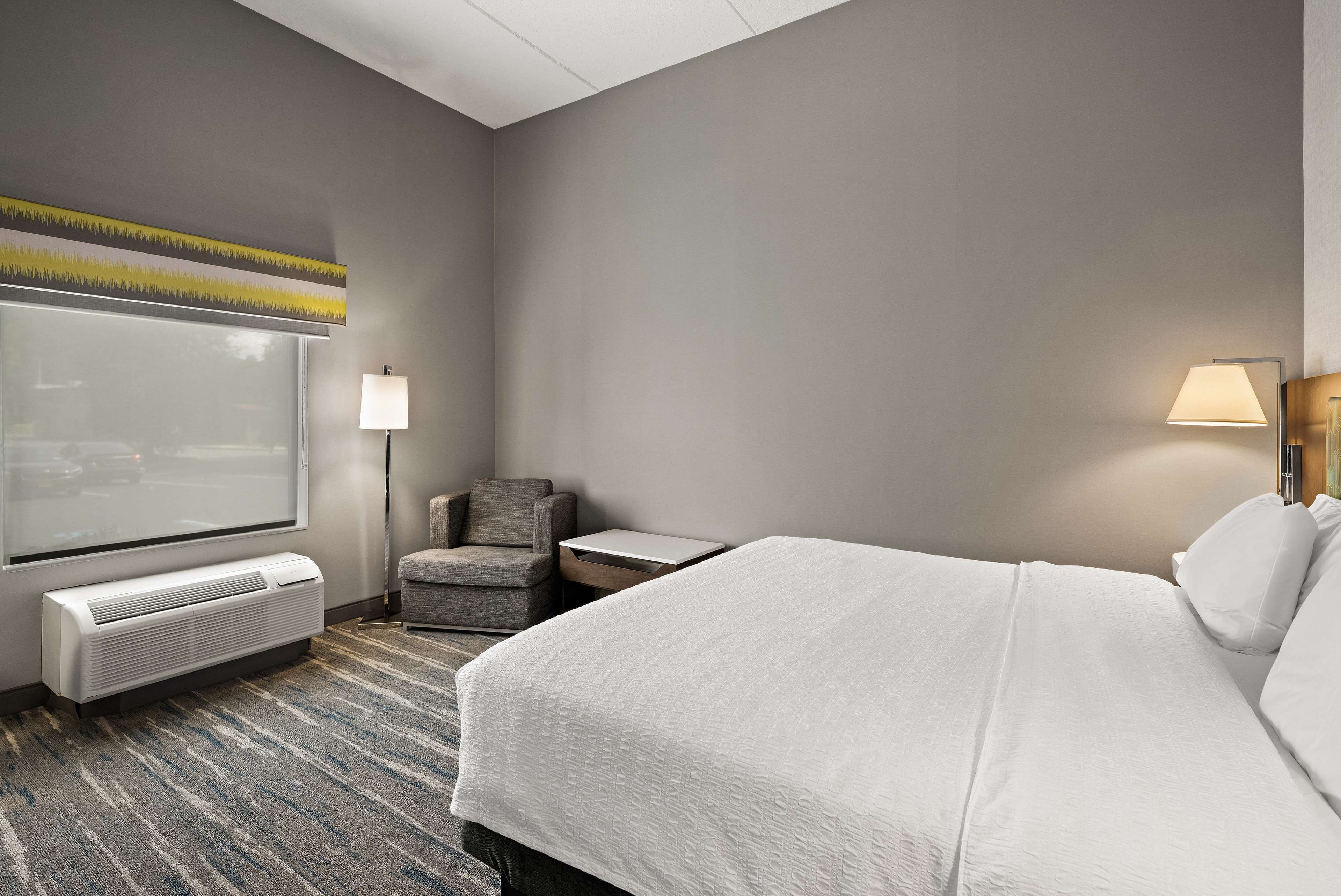 Quarto de hotel com cama grande, uma cadeira, escrivaninha e janela com vista para a rua.