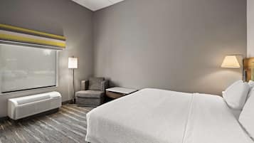 Quarto de hotel com cama grande, uma cadeira, escrivaninha e janela com vista para a rua.